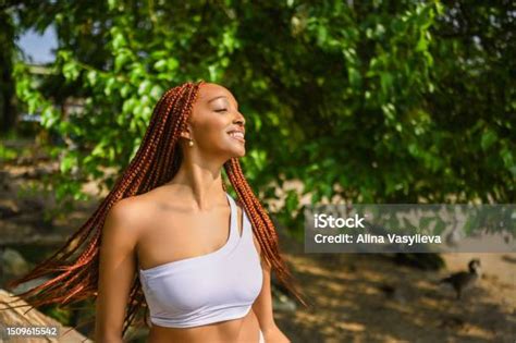 자연의 아름다운 젊은 아프리카계 미국인 여성의 긴 빨간 머리띠 머리 스타일과 완벽한 하얀 치아 미소 녹색 단풍 해변 배경으로 화창한 여름날 수영복을 입고 포즈를 취하는 야외