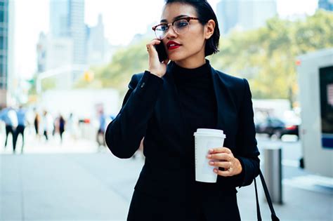뉴욕 거리 붉은 입술을 들고 커피 테이크 아웃 사무실에가 휴대 전화 대화로 자신감 사업가에 걷고 있는 동안 모바일에 얘기 하는 세련 된 안경에 심각한 여성 관리자 Stem