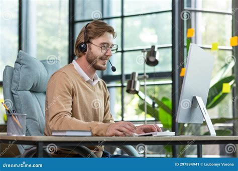 Handsome Male Programmer Sits In A Headset In The Office At The Table In Profile Works At The