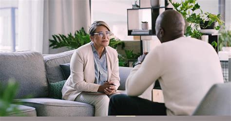 심리학자 치료 및 외로움 조언 및 정신 건강을 위한 사무실의 성숙한 여성 여성 우울증 상담 및 부채 또는 슬픔을 위한 테이블이 있는 직장의 상담 및 소파 남성에 대한 스톡