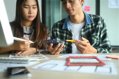 Designers Discussing User Interface Ideas While Reviewing A Smartphone And Design Sketches On