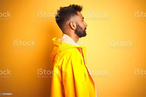 고립된 노란색 배경 위에 서있는 비옷을 입은 젊은 인도 남자는 자신감을 가지고 자연스러운 얼굴로 프로필 포즈를 취합니다 가을에