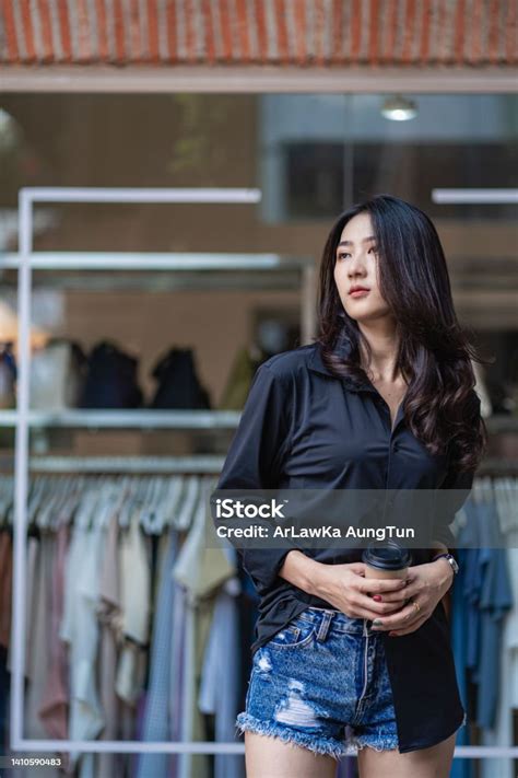 검은 셔츠에 커피 한 잔을 들고 있는 아름다운 아시아 여성이 행복하게 웃으며 홀리데이 컨셉 빌딩 앞에 서 있다 갈색 머리에 대한 스톡 사진 및 기타 이미지 Istock