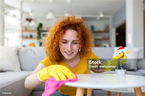 아름다운 젊은 여성이 집을 청소합니다 소녀는 먼지를 문지른다 넝마와 스프레이 병 세제로 청소하는 고무 보호 노란색 장갑을 착용 한 웃는 여성 가정 가사 개념 가사 집안일에