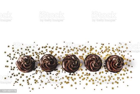 초콜릿 아이싱과 골드 스파클이 있는 골드 컵케이크는 황금별 모양의 색종이가 있는 흰색 배경에 반짝입니다 휴일 개념 디자인의 배경입니다 플랫 레이 스타일 공간을 복사합니다 0