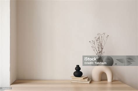 예술적인 인테리어 정물 현대 유기물 기하학적 모양의 조각품 마른 꽃 풀 나무 탁자 위에 오래된 책이 있는 꽃병 홈 스테이징 최소한의 장식 개념 빈 베이지색 벽 배경 벽에