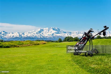 골프 코스의 페어웨이 가장자리에 가방과 골프 클럽이있는 골프 카트 배경에서 알프스 몬테 로사 체인 이탈리아 측에서 볼 수