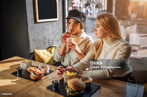 두 아름 다운 청소년 카페에서 테이블에 앉아서 왼쪽을 보세요 처음 마시는 칵테일 친구 외 두 번째 앉아입니다 그들은 Aat 창입니다 밖에 서 일 Shiines입니다 갈색