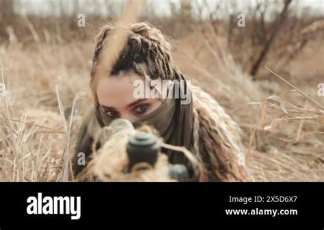 A Sniper Woman Is Seen Peering Through The Optical Scope Of Her Rifle As The Camera Pans From