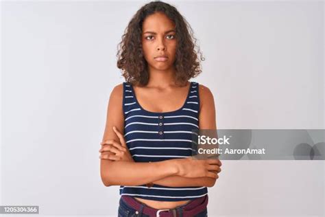 줄무늬 티셔츠를 입은 젊은 브라질 여성이 고립된 흰색 배경에 서 있고 긴장하고 두 팔을 교차한 얼굴표정에 불만을 품었다 부정적인 사람 T 셔츠에 대한 스톡 사진 및 기타