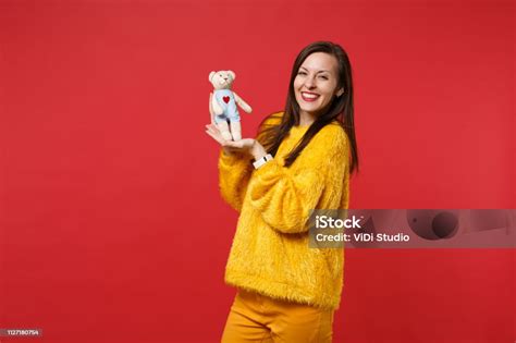 스튜디오에서 밝은 빨간 벽 배경에 고립 된 테 디 베어 봉 제 장난감을 들고 노란색 모피 스웨터에서 즐거운 젊은 여자의 초상화 사람들이 진심으 감정 라이프 스타일 개념 복사