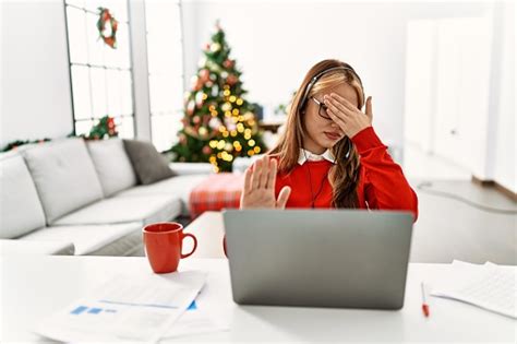 어린 백인 소녀는 손으로 눈을 가리고 슬프고 두려움표정으로 제스처를 멈추고 크리스마스 트리로 노트북을 사용하여 작업합니다 부끄럽고 부정적인 개념 크리스마스에 대한 스톡 사진