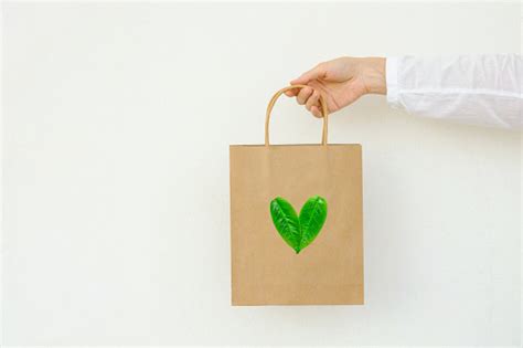 젊은 백인 여자는 흰색 벽 배경에 갈색 공예 종이 가방을 손에 빈 빈 조롱을 보유 하 고 있습니다 나뭇잎에서 하트 로고입니다 환경 보전 재활용 플라스틱 무료 개념 가방에