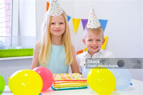 두 금발 백인 아이 소년과 생일 모자에 여자 카메라를보고 생일 파티에서 미소 풍선과 생일 무지개 케이크 다채로운 배경 가족에 대한 스톡 사진 및 기타 이미지 Istock
