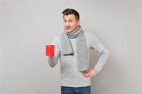 회색 스웨터 스카프 지주 빨간 컵 커피 또는 차 스튜디오에 회색 배경에 고립의 젊은 남자를 놀 랐 다 건강 한 라이프 스타일
