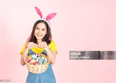 토끼 귀를 입고 사랑스러운 미소와 파스텔 배경에 고립 된 화려한 장식 의상과 나무 바구니에 화려한 부활절 달걀을 들고 아시아 아름다움 행복 젊은 여성의 절반 길이 스튜디오