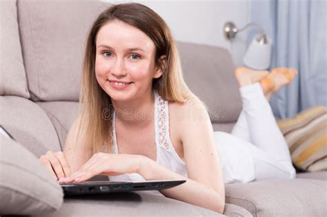 Portrait Of Cheerful Female Who Is Working With Laptop On Sofa Stock