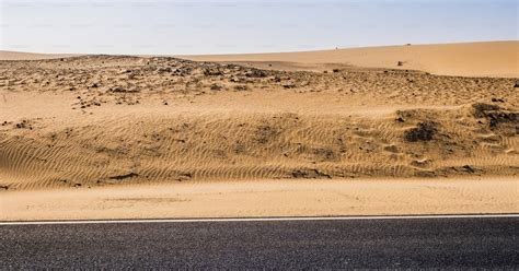 왼쪽과 오른쪽에 모래 언덕과 사막이 있고 배경에 푸른 하늘이 있는 검은 아스팔트 도로 나쁜 기후 변화 미래로 인해 건조한 사막 세계의 여행 개념 물 비상 행성 사진