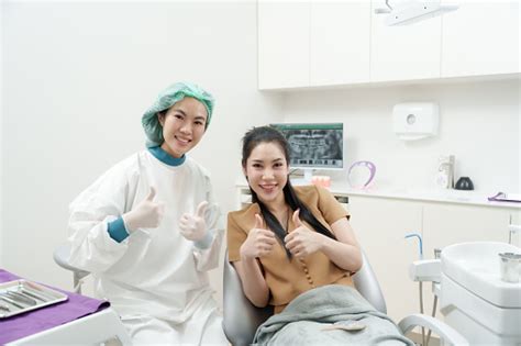 아시아 여성 치과 의사와 성인 여성 환자가 엑스레이 모니터를 배경으로 현대 치과 진료소에서 성공적인 치과 치료를 받은 후 엄지손가락을 치켜세우고 미소를 지으며 함께 포즈를