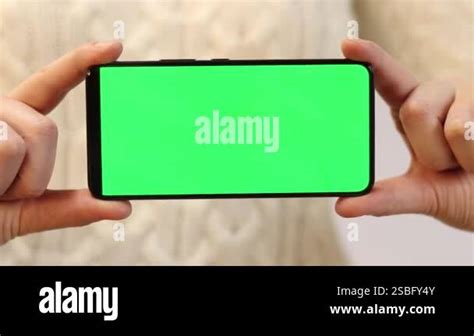 Hand holding a phone with a green screen. Woman in a white sweater ...