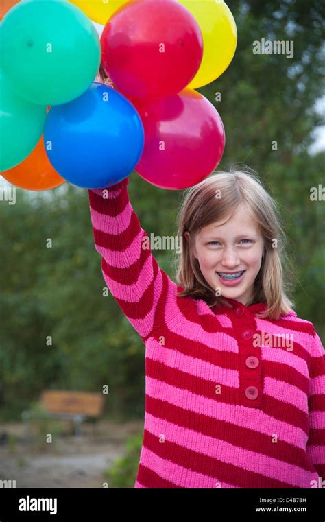 Smiling Young Girl Wearing Braces And Holding A Bunch Of Balloons Up