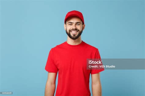 파란색 벽 배경 스튜디오 초상화에 고립 된 빨간색 유니폼 작업복을 입은 배달 남자 택배 딜러로 일하는 캡 티셔츠 프린트의 전문 남성 직원 서비스 개념 복사 공간을 모의합니다
