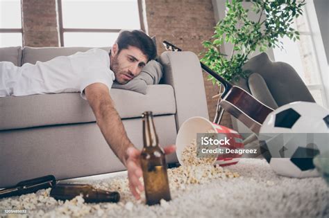 바닥에 맥주 병 팝콘을 복용 소파 누워 혼합 경주 술남자의 사진은 파티 숙취 아침 두통 지저분한 평면 실내 후 고통 미친 엔터테인먼트를했다 갈색 머리에 대한 스톡 사진 및