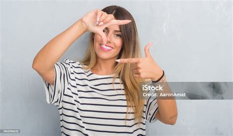 그런 지 위에 젊은 성인 여자 회색 벽 손으로 만드는 프레임 및 행복 한 얼굴로 손가락을 웃 고 해군 티셔츠 입고 창의력과 사진