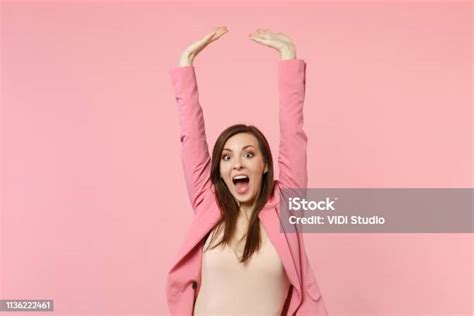 스튜디오에서 파스텔 분홍색 벽 배경에 고립 된 입 넓은 오픈 상승 손을 유지 쾌활 한 재미 아름 다운 젊은 여자의 초상화