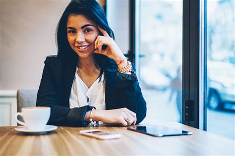 식당에서 여가 시간을 보내는 동안 카메라 보고 웃는 귀여운 여자 사람의 자른된 이미지 실내 나무 테이블에 앉아 휴식 하는 젊은 성공적인 사업가의 반 길이 초상화 귀여운에
