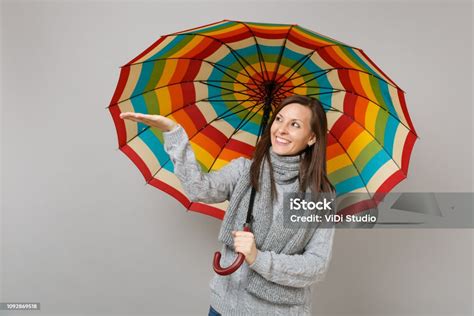 회색 스웨터에 젊은 여자를 웃 고 회색 벽 배경에 고립 된 화려한 우산을 들고 가리키는 손 스카프 건강 패션 라이프 스타일 사람 감정 추운 계절 개념 복사 공간을 비웃는 다