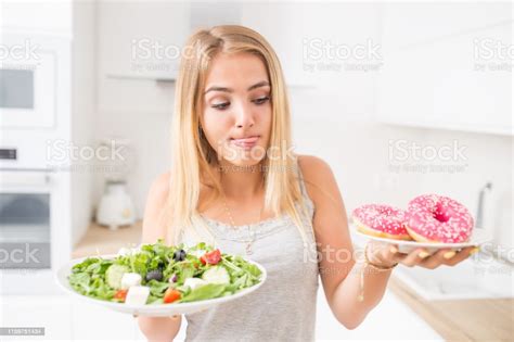 집에서 부엌에서 아침 이나 저녁 식사에서 젊은 금발 소녀는 도넛과 야채 샐러드 중에서 선택합니다 개념에 대한 스톡 사진 및 기타 이미지 Istock