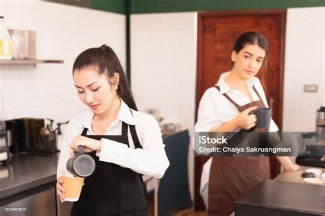 아시아 바리스타 여성들이 우유를 테이크아웃 핫 커피 컵에 채우고 백인 바리스타 여성은 카페 커피숍에서 고객을 위해 커피를 준비하기 위해 그녀를 바라본다 2명에 대한 스톡
