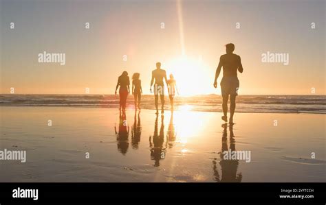Group Of Friends In Swimwear Walk Towards Waves At Sunset On Summer
