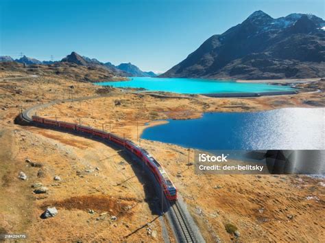 가을에는 푸른 산 비앙코 호수 눈 덮인 바위 푸른 하늘 근처의 현대적인 빨간 기차의 공중 전망 베르니나 익스프레스 스위스 알프스의 기차 철도 가을의 오렌지 언덕의 평면도 0