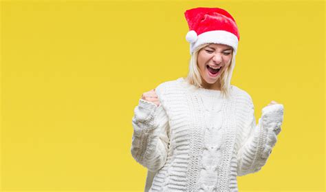 젊은 아름 다운 금발 여자 매우 행복 하 고 흥분 무기와 우승자 제스처를 하 고 격리 된 배경 위에 크리스마스 모자를 쓰고 웃