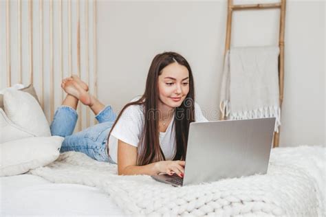 Young Woman Lying On Her Stomach In Bed Work On Laptop And Takes Online