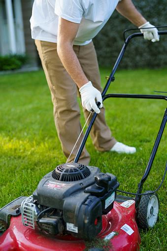 보호 장갑을 낀 알아볼 수 없는 정원사 남자가 뒤뜰의 푸른 잔디를 깎기 전에 잔디 깎는 기계를 시작합니다 기체 물리 구조에 대한 스톡 사진 및 기타 이미지 Istock