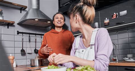 테이블에서 샐러드를 준비하는 동안 절친과 이야기를 나누는 다인종 여성의 허리 초상화 부엌에서 친구와 함께 요리하는 소녀 그녀의 가장 친한 친구는 무언가를 말하고 웃는다