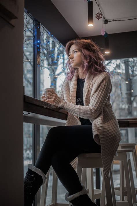 Girl In A White Sweater Sits In A Cafe And Looks Out The Window Stock