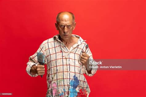 카메라 앞에 브러시가 서 있는 성숙한 또는 수석 회색 화가 빨간 에 고립 된 주위에 속이는 페인트 얼룩 진 셔츠를 입은 재미있는 남자 60 64세에 대한 스톡 사진 및 기타