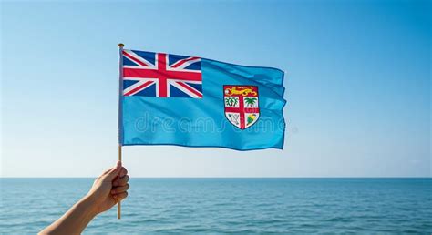 Hand Holding The Flag Of Fiji Against A Clear Blue Sky And Ocean Stock