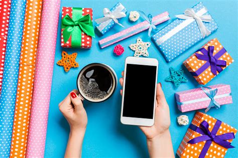 한 손에는 휴대폰을 들고 있는 여성의 모습이고 다른 손에는 파란색 배경에 커피 한 잔을 들고 있는 모습 크리스마스 장식 및 장난감 연말연시 컨셉입니다 Mockup 가정