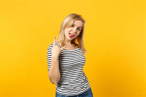 노란색 주황색 배경에 고립 된 무거운 금속 바위 기호 록 앤 롤 묘사 혀를 보여주는 줄무늬 옷에 재미 있는 젊은 여자 사람들은 진심으로 감정 라이프 스타일 개념입니다 복사