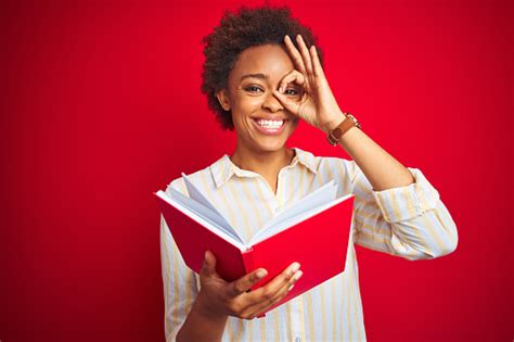 빨간 고립 된 배경을 통해 책을 읽는 아프리카 계 미국인 여성 행복한 얼굴 미소 와 함께 확인 기호를 하고 눈으로 손가락을 통해 보고 개념에 대한 스톡 사진 및 기타 이미지