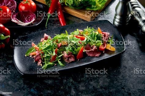 구운 쇠고기와 신선한 채소를 곁들인 따뜻한 샐러드는 대리석 배경의 검은 접시에 담겨 제공됩니다 레스토랑 음식 클로즈업 선택적 초점 건강한 식생활에 대한 스톡 사진 및 기타
