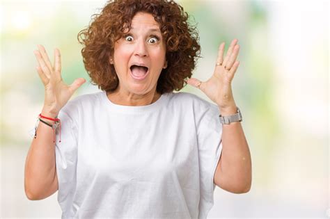 아름 다운 중간 어른 고위 여자에 흰색 티셔츠를 입고 미친 축 하 배경 절연 및 팔 제기 성공을 위한 놀라게 했 고 눈 흥분 비명 우승자 개념 T 셔츠에 대한 스톡 사진 및