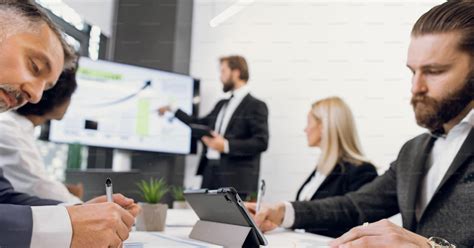 두 사람은 다양한 사업가에 집중하여 남성 연사의 연설을 들으면서 메모를 작성하고 사무실 회의에서 다양한 직원 그룹에 재무 프레젠테이션을 보여주었습니다 태블릿과 휴대폰에