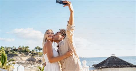 사랑에 빠진 행복한 커플은 해변에서 스마트폰과 함께 셀카를 찍고 있다 밀월 여행하다 휴가 관광객 플라야 델 두케 테네리페 사진 Unsplash의 키스 이미지