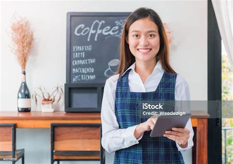 아시아 여성 바리 스타 블루 착용 앞치마 보유 고객 커피 사업 소유자 개념에서에서 카페 대기 순서로 얼굴을 미소와 함께 태블릿 컴퓨터 커피 메뉴 고객에 대한 스톡 사진 및